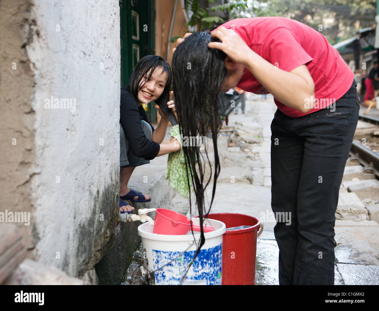 Two young girls wash their hair by the railway track that runs through ...
