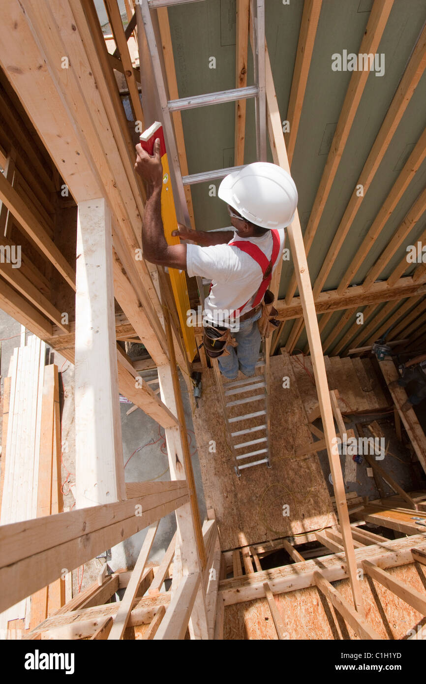 Hispanic carpenter carrying a level up ladder to second floor at a ...