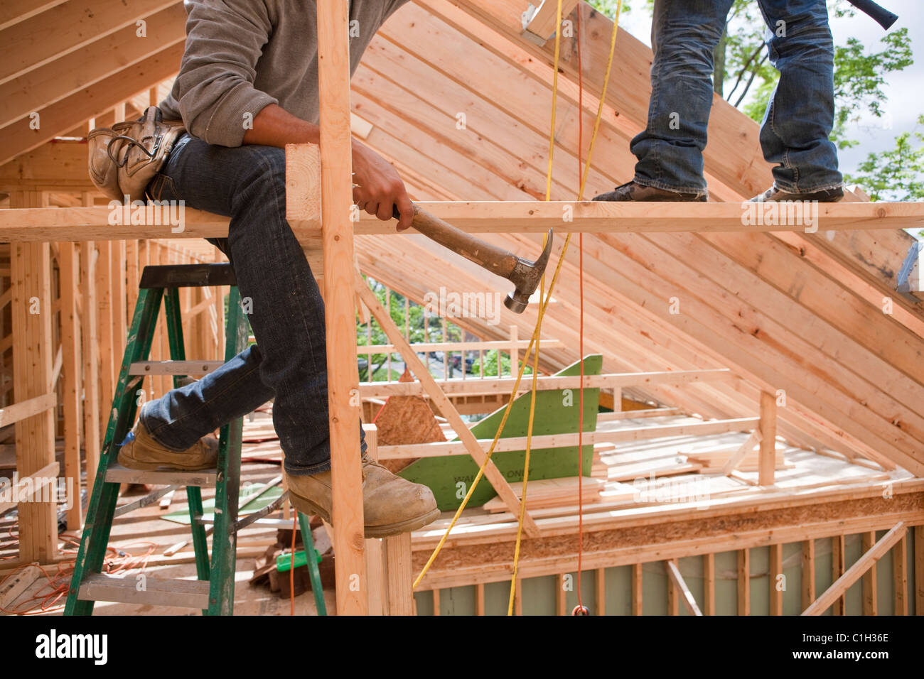 Hispanic carpenters working on upper floor from a beam at a house under ...