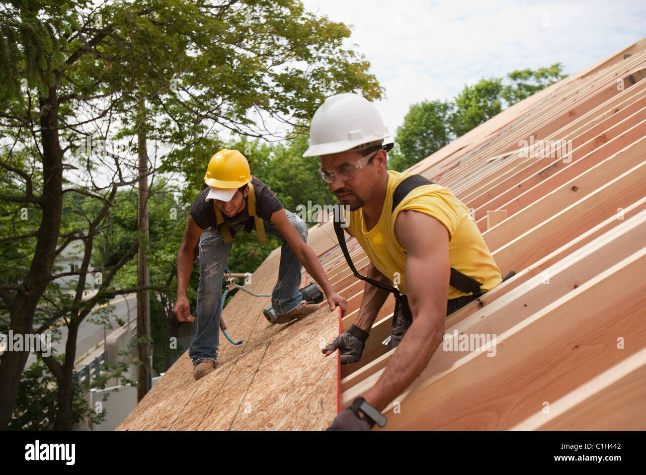 Hispanic carpenters placing roof panel at a house under construction ...