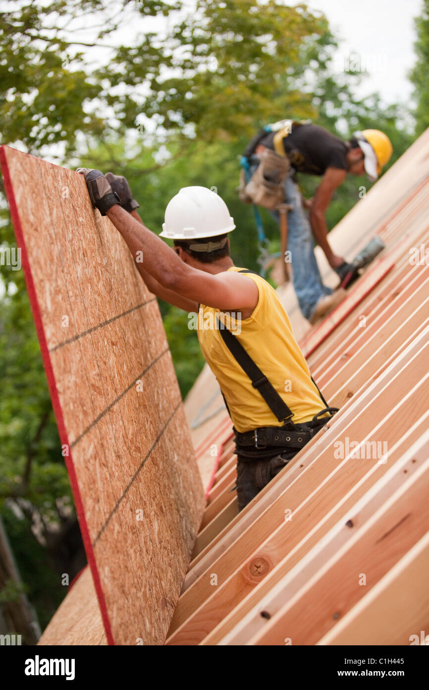 Hispanic carpenters placing roof panel at a house under construction ...