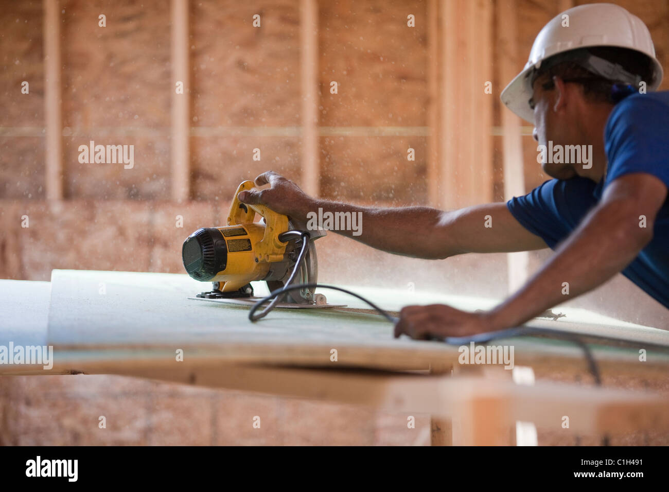 Hispanic carpenter using circular saw on roofing sheathing at a house ...