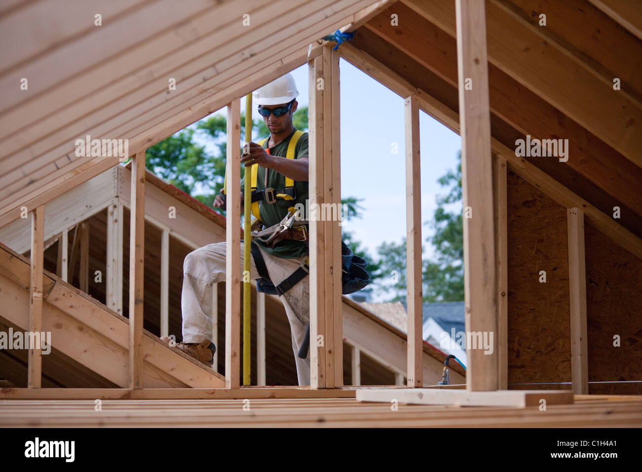 Hispanic carpenter measuring wall studs at a house under construction ...