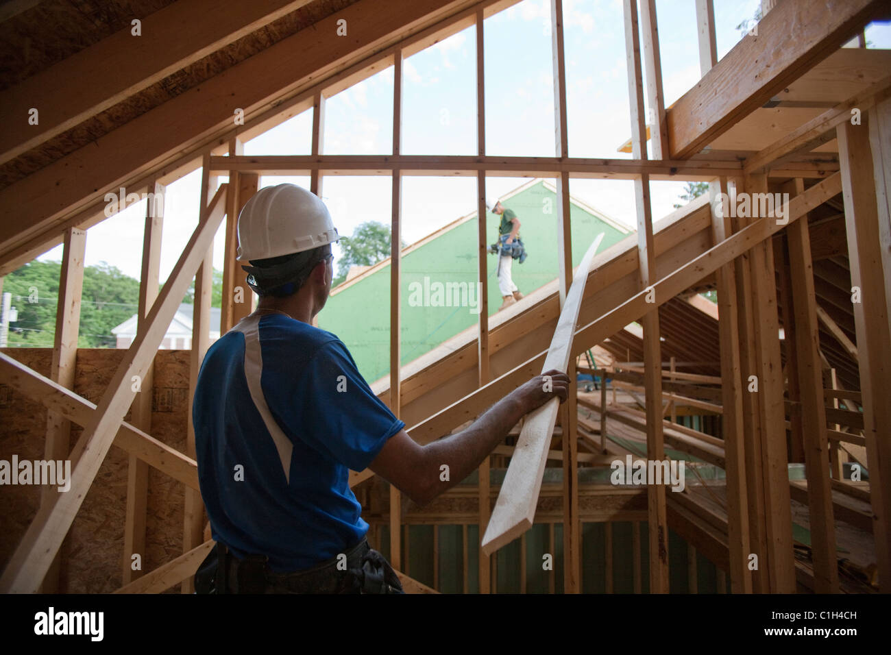 Hispanic carpenters bringing construction trim strip up to roof of a ...