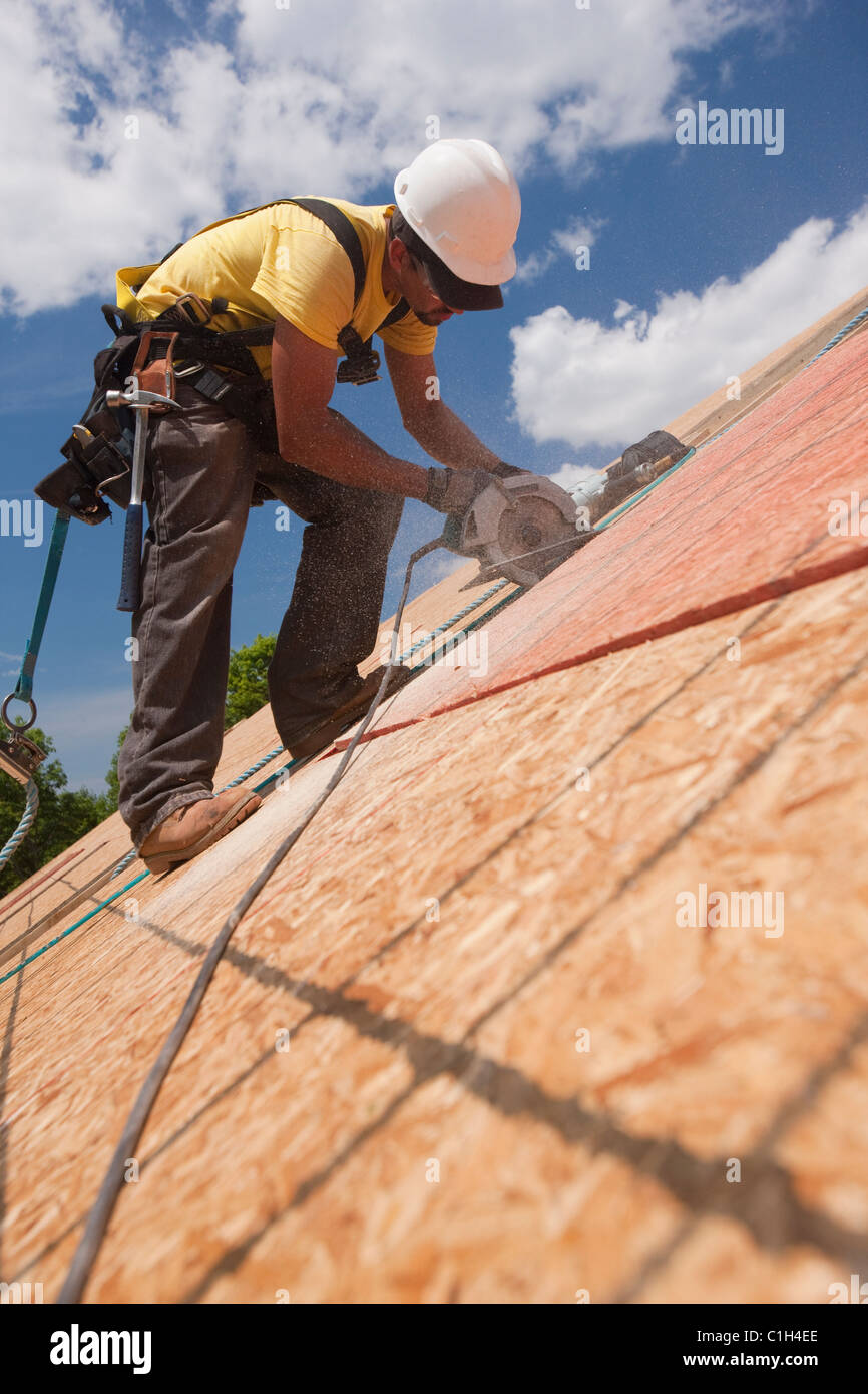 Carpenter using a circular saw on the roof panel at a house under ...