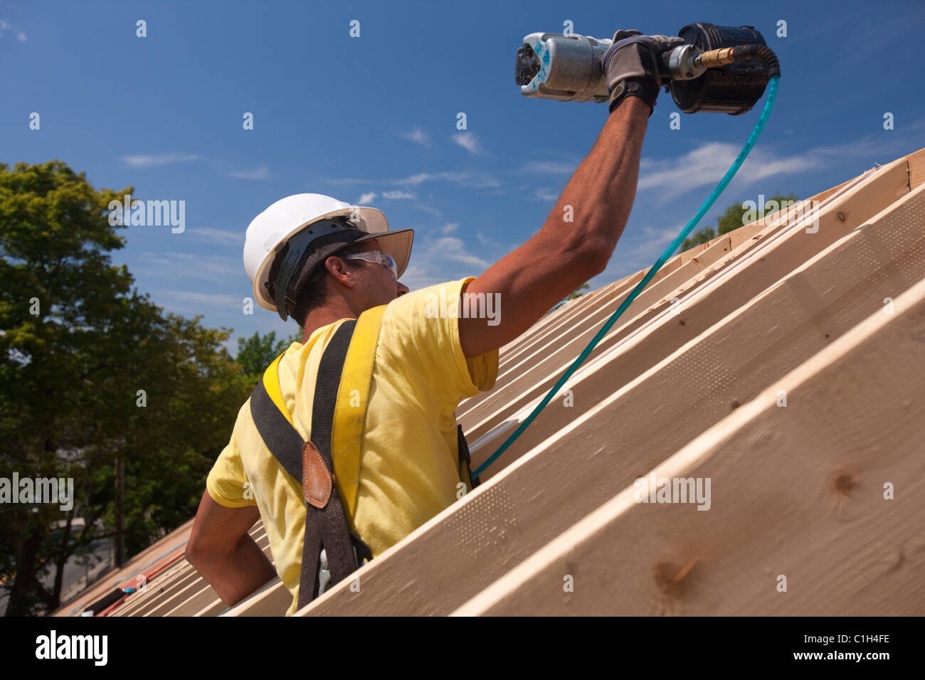Hispanic carpenter using nail gun on roofing at a house under ...