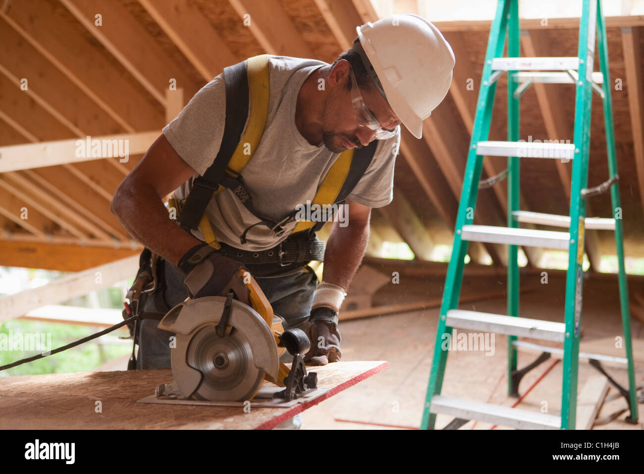 Hispanic carpenter using a circular saw on roof panel at a house under ...