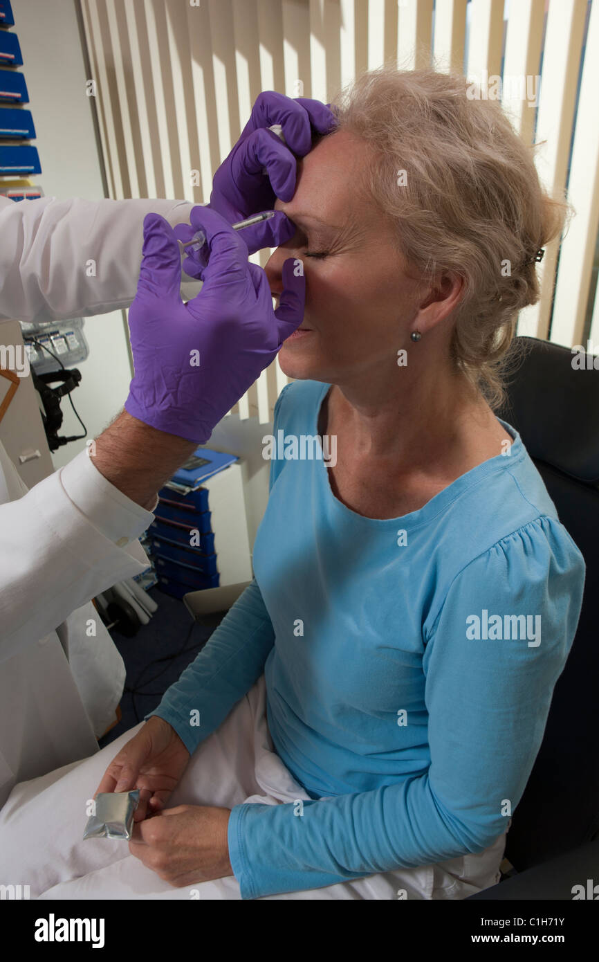 Ophthalmologist giving a Botox injection on the forehead of a patient ...