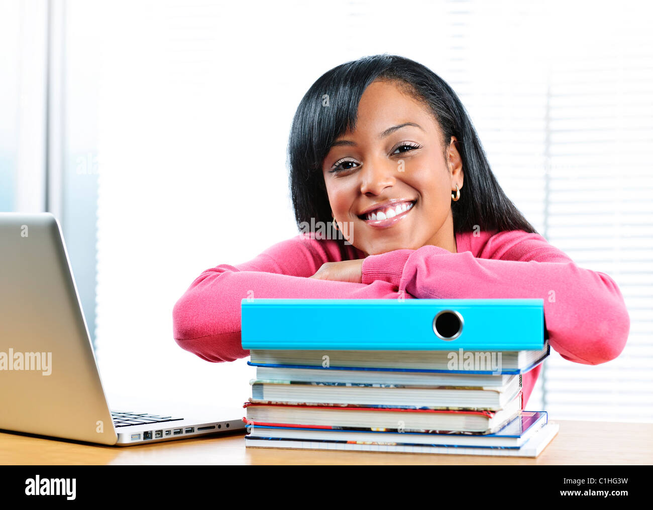 Smiling young black female student with textbooks at desk Stock Photo ...