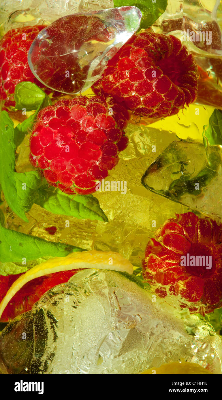 Extreme closeup of a yellow cocktail drink with raspberries and mint ...