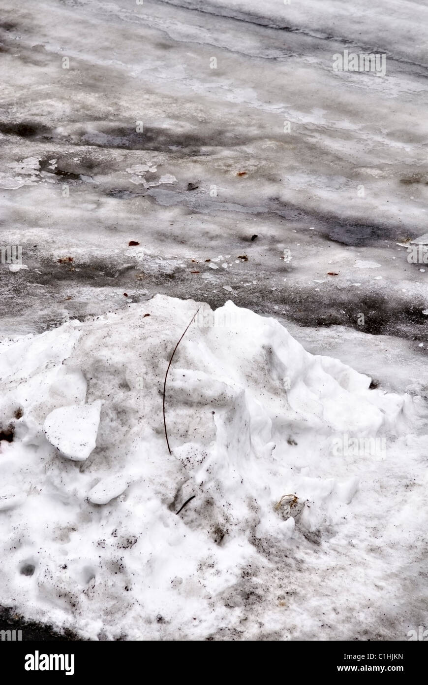 Pile of dirty thawing snow slush and ice with tyre tread on the road ...