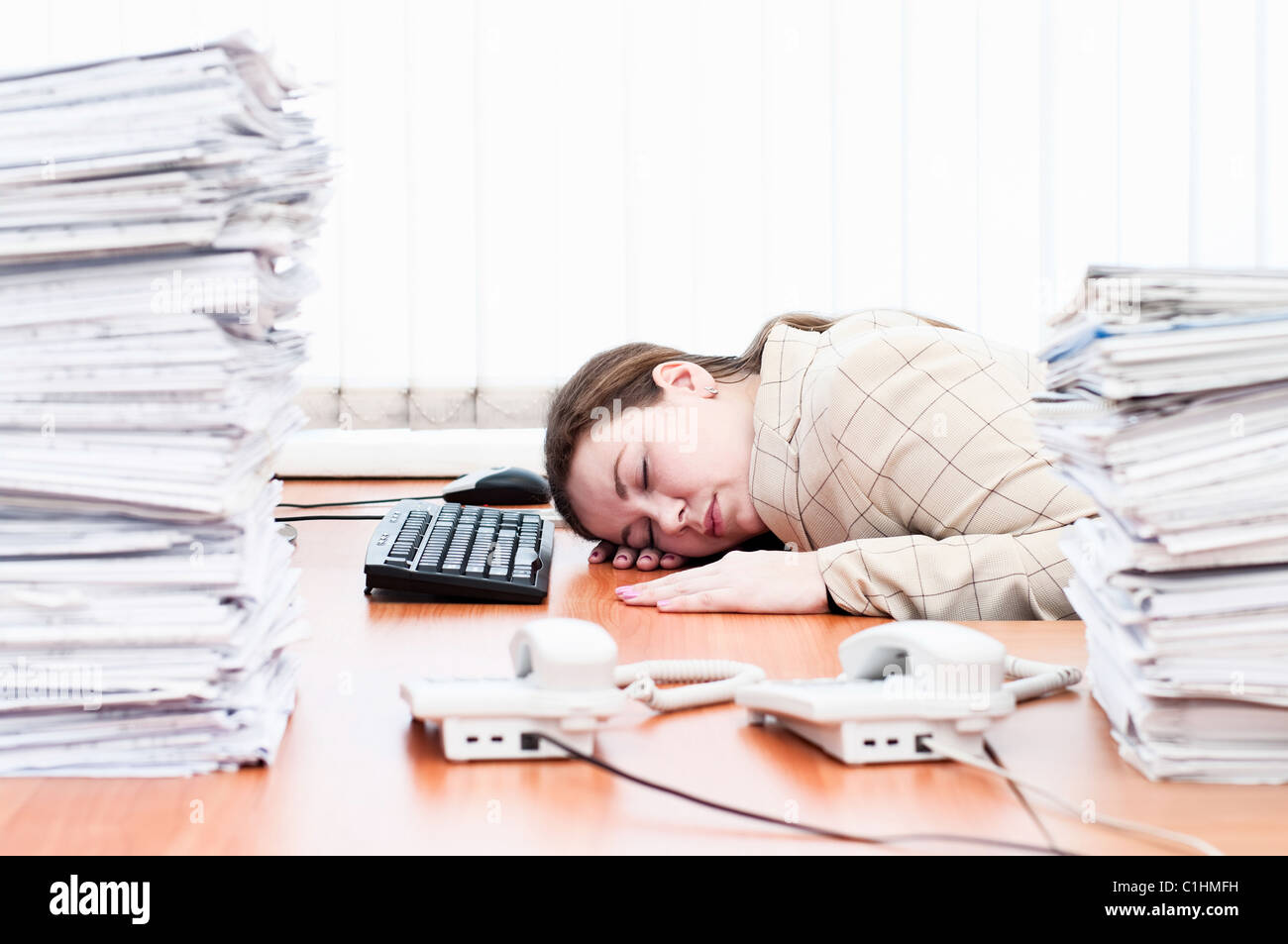 Caucasian woman sleeping on working place in office room between piles ...