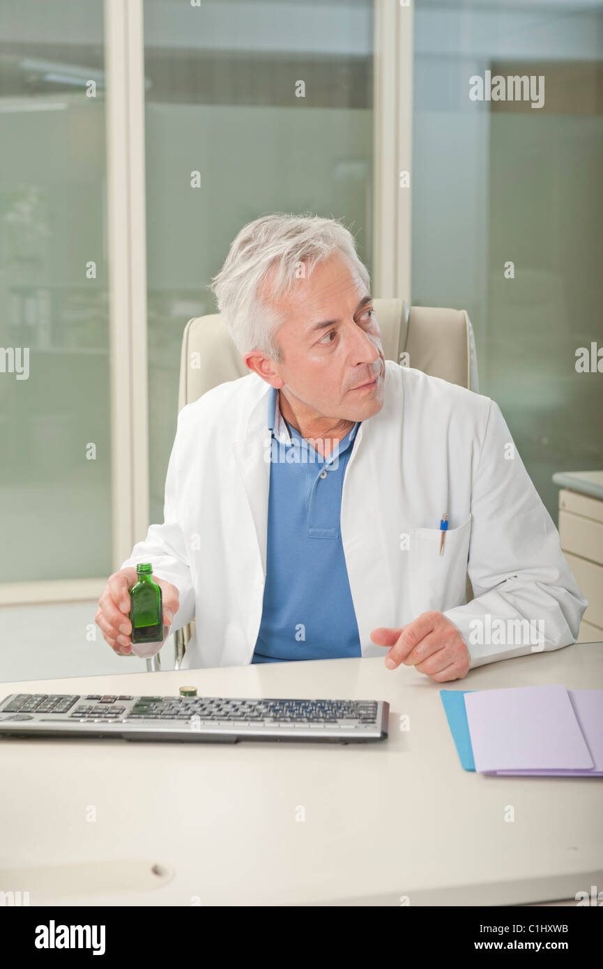 Doctor at desk drinking liquor secretly Stock Photo - Alamy