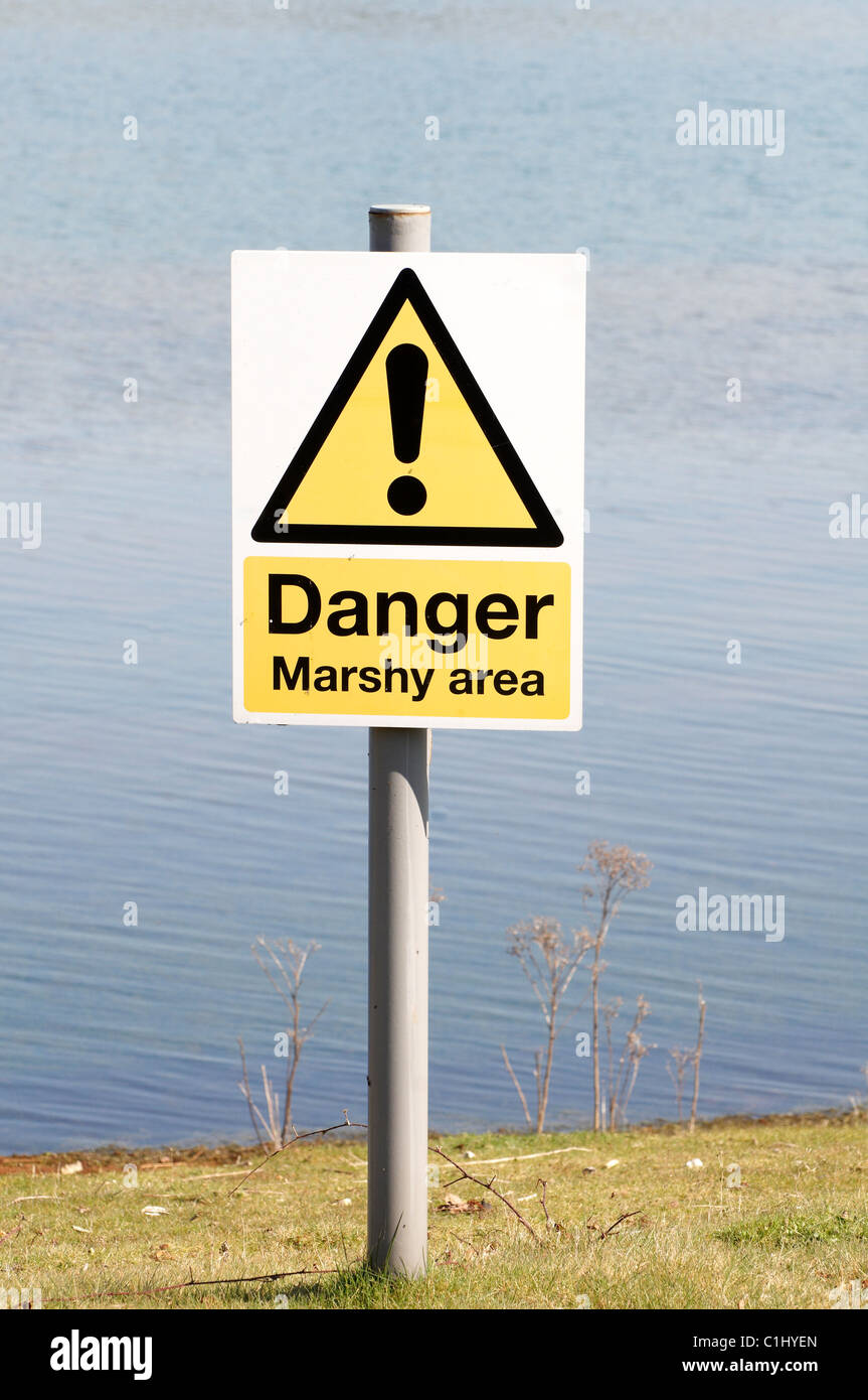 Warning sign indicating danger in a marshy area by a man-made lake ...