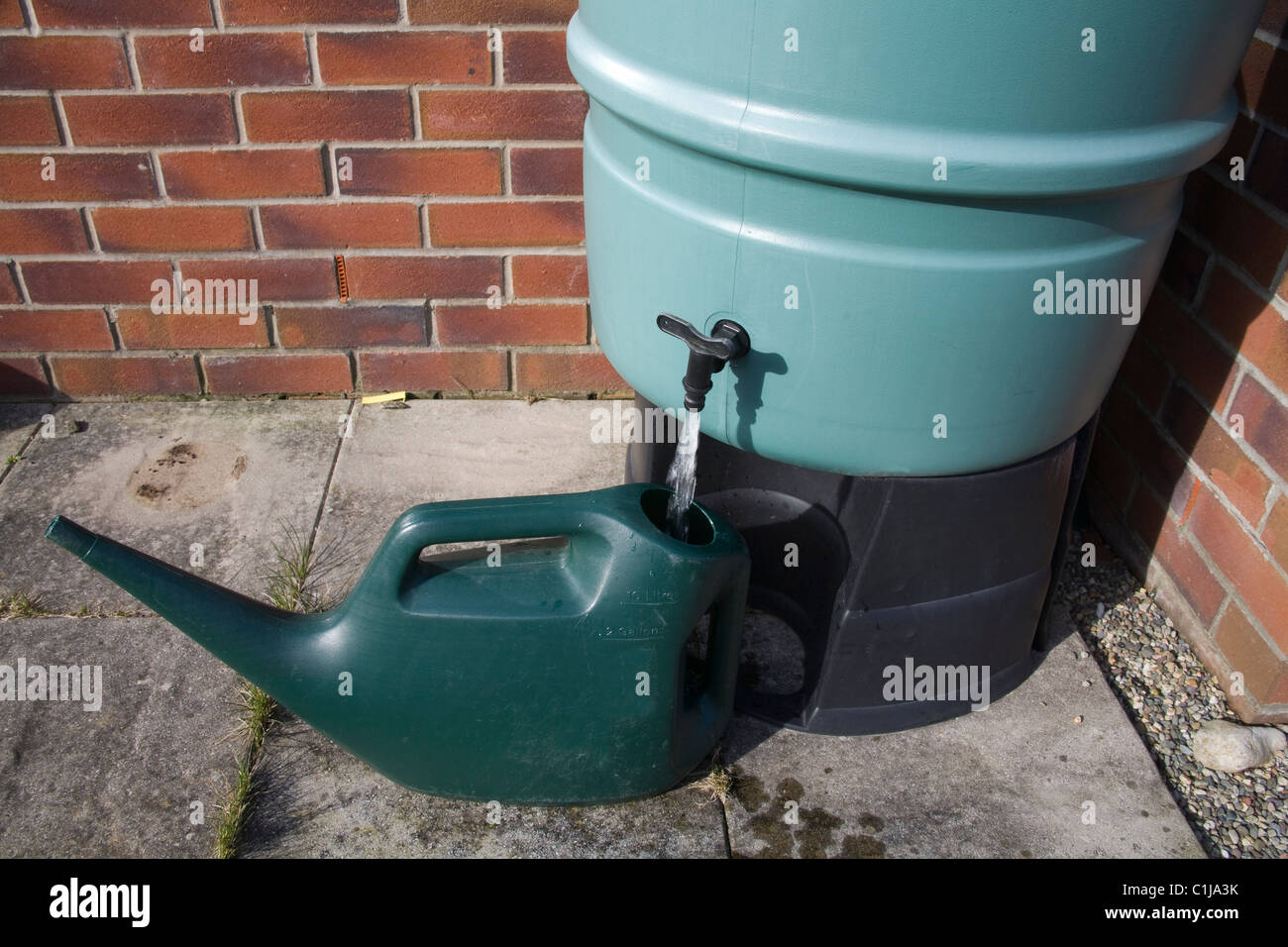 Filling up a watering can from harvested rain water in a green water ...