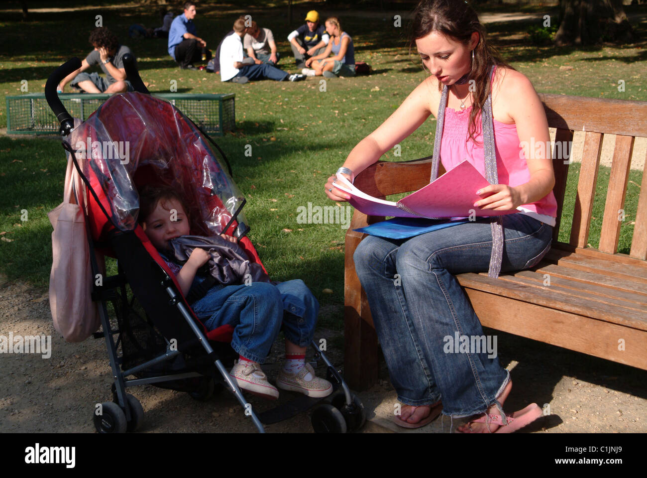 Young female student in a park writing in a notebook while her child ...