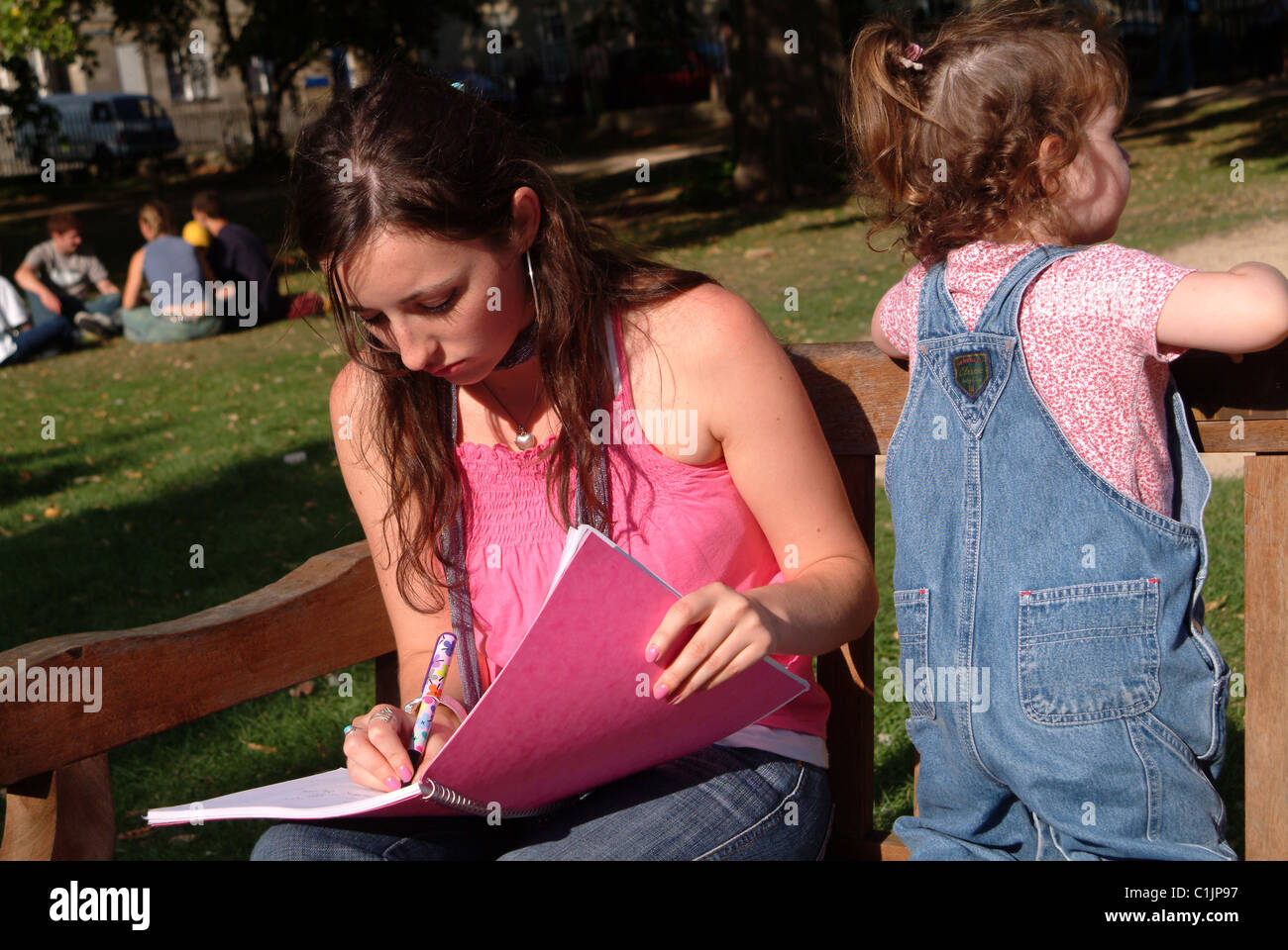 Young female student sitting in a park doing paperwork while her child ...