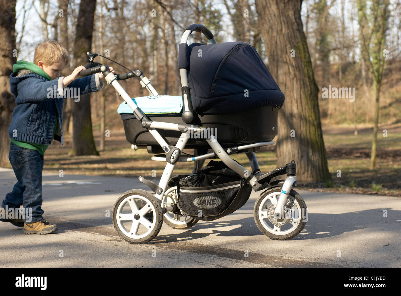 Child blond boy pushing stroller with sister in park Stock Photo - Alamy