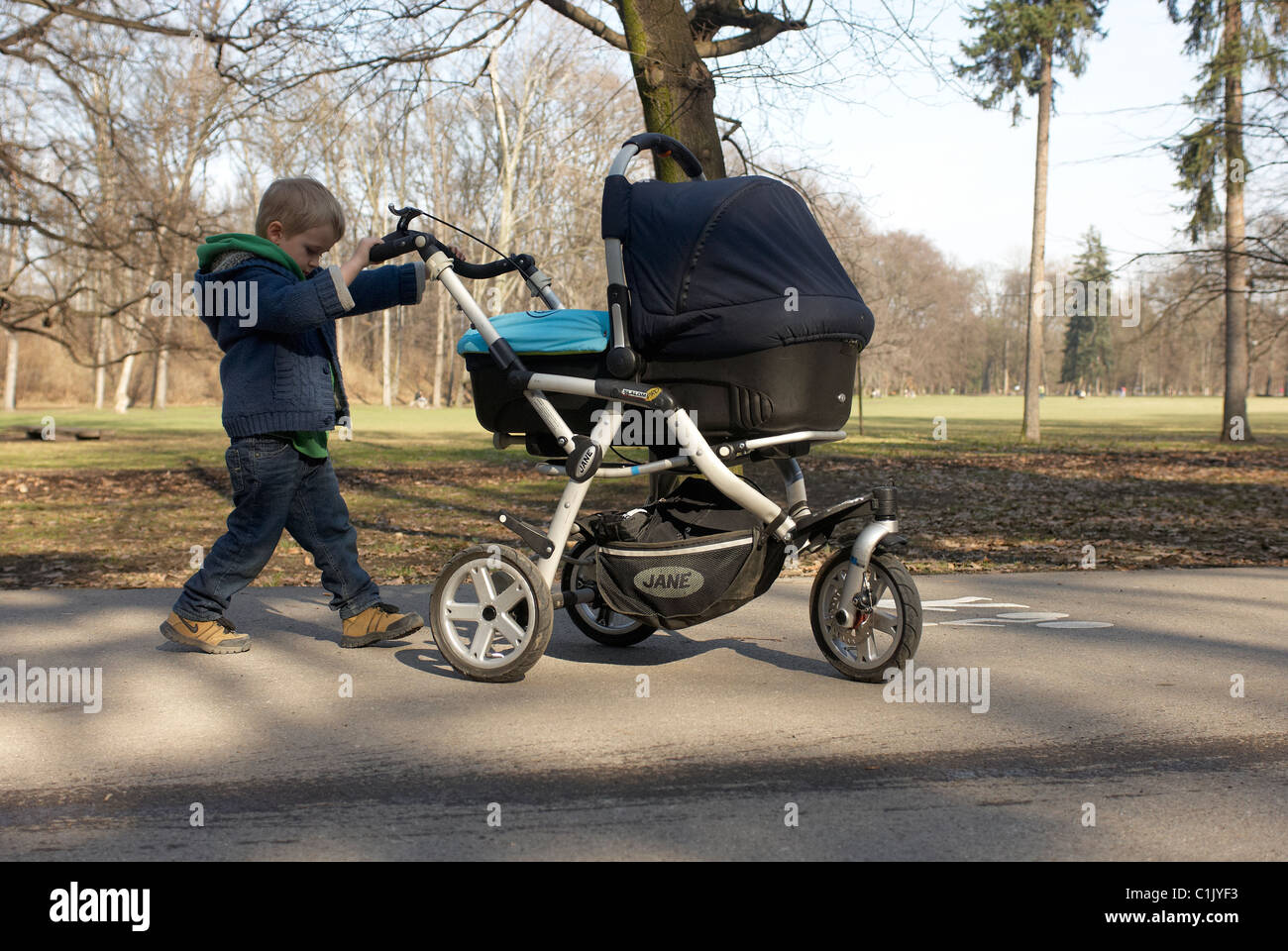 Child blond boy pushing stroller with sister in park Stock Photo - Alamy