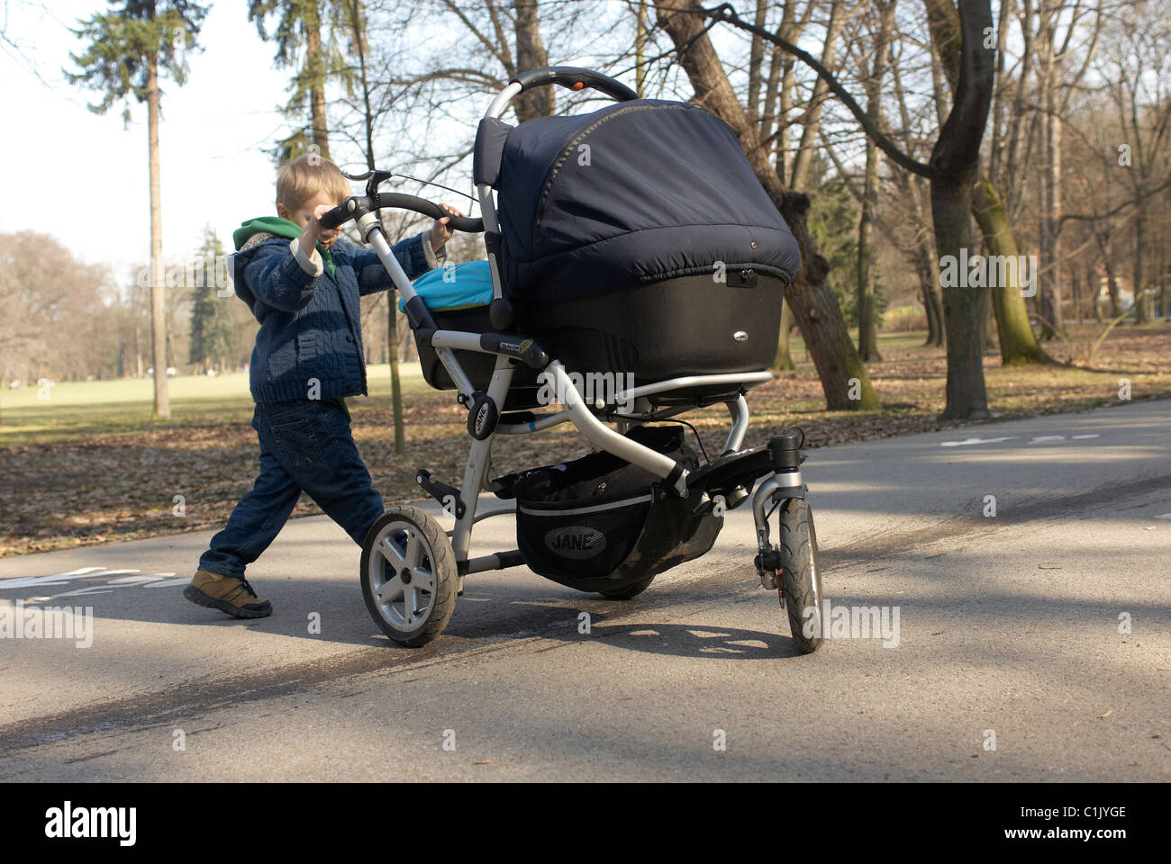 Child blond boy pushing stroller with sister in park Stock Photo - Alamy