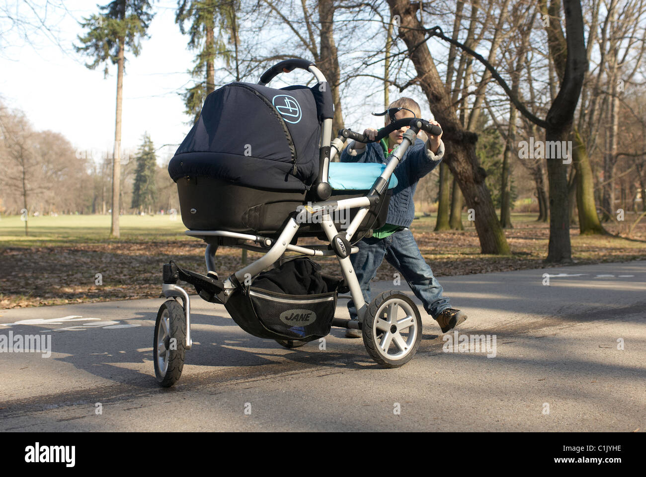 Child blond boy pushing stroller with sister in park Stock Photo - Alamy