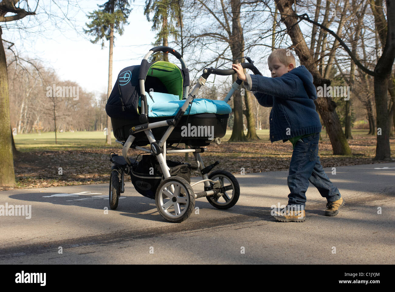 Child blond boy pushing stroller with sister in park Stock Photo - Alamy