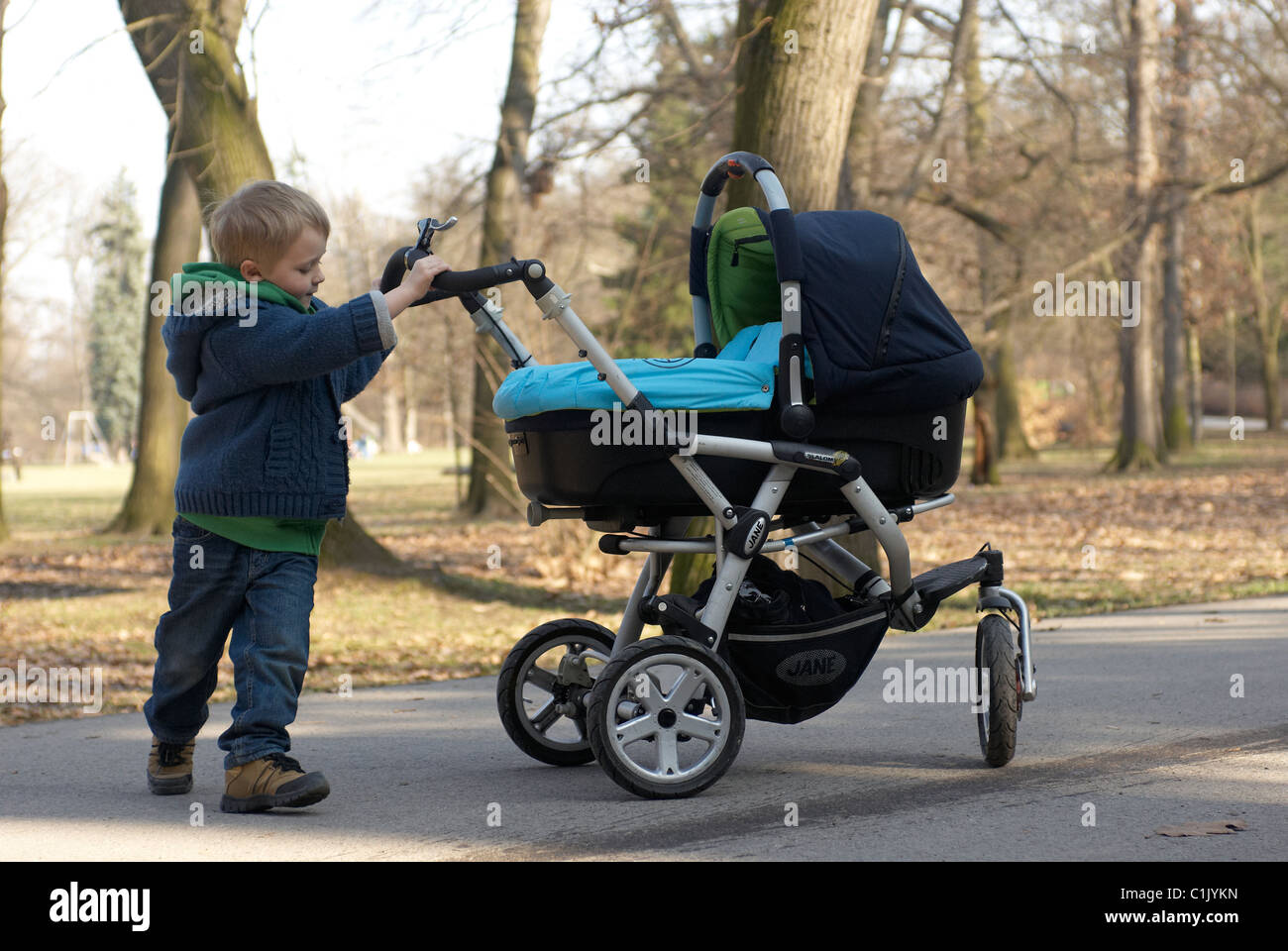 Child blond boy pushing stroller with sister in park Stock Photo - Alamy