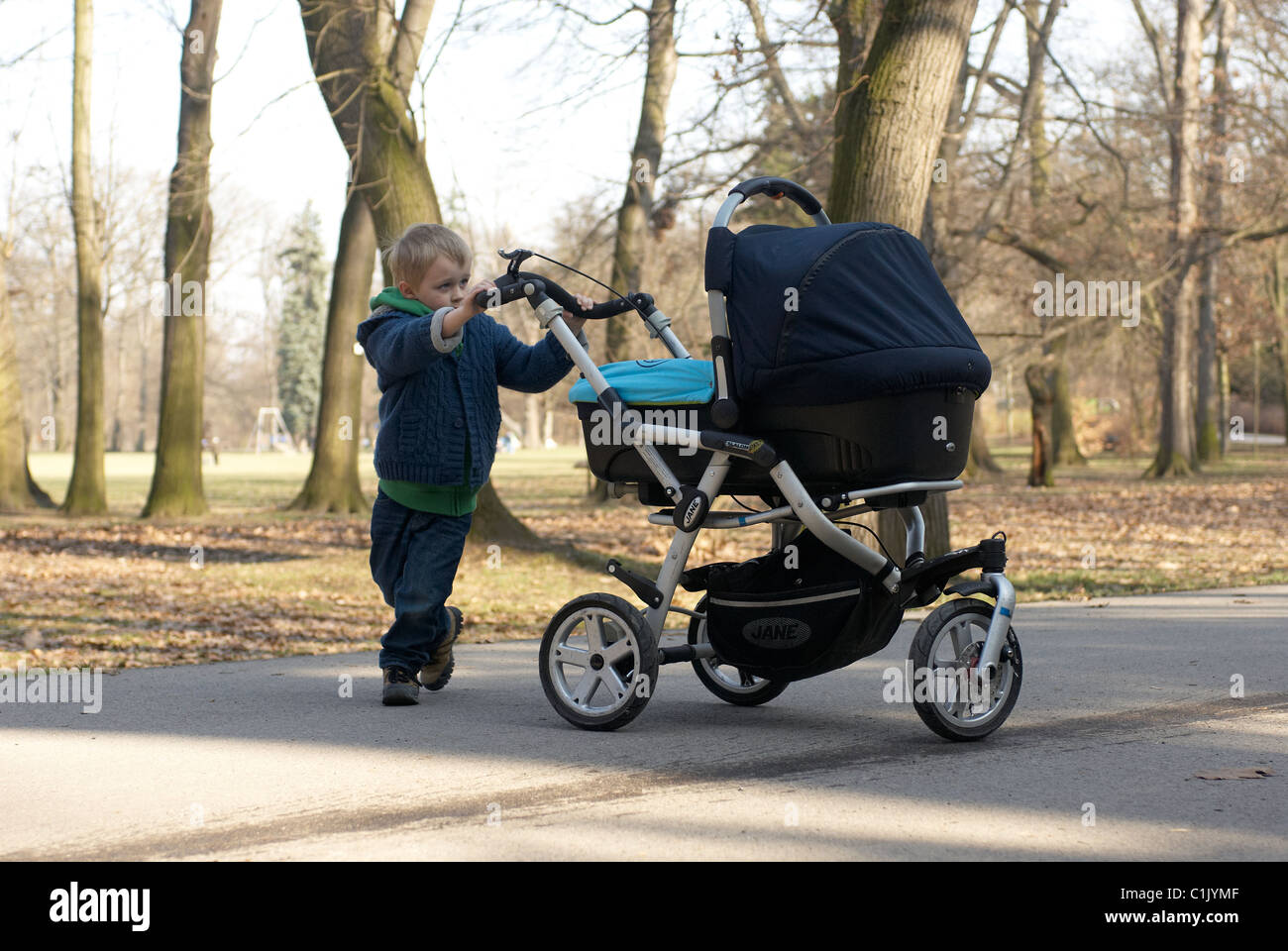 Child blond boy pushing stroller with sister in park Stock Photo - Alamy