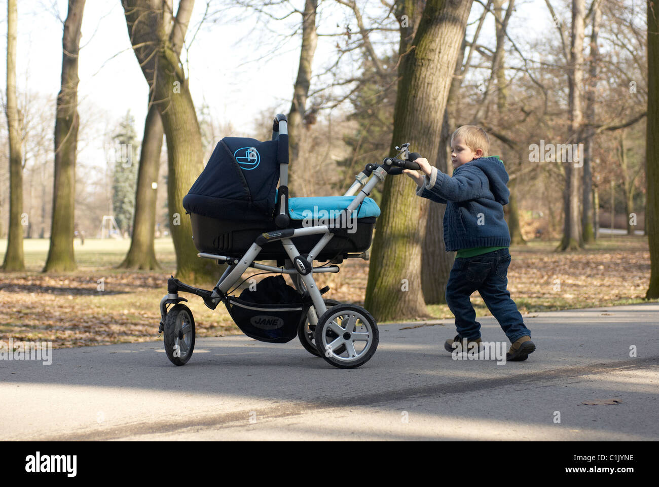 Child blond boy pushing stroller with sister in park Stock Photo - Alamy
