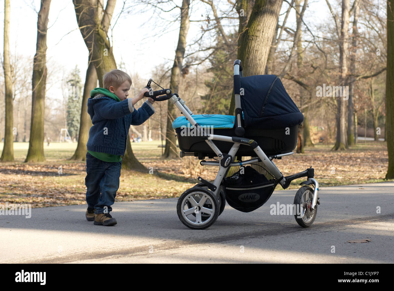 Child blond boy pushing stroller with sister in park Stock Photo - Alamy