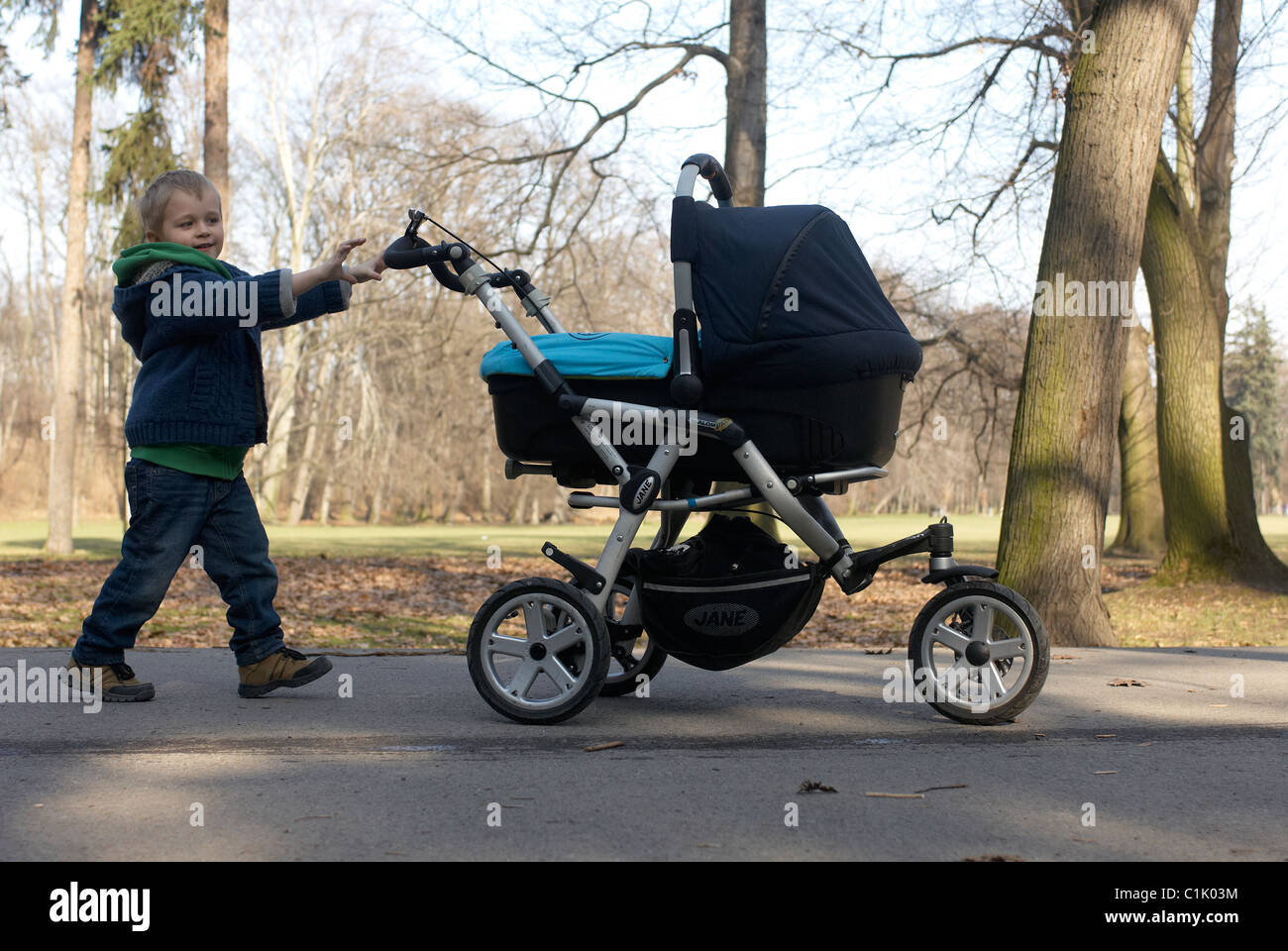 Child blond boy pushing stroller with sister in park Stock Photo - Alamy
