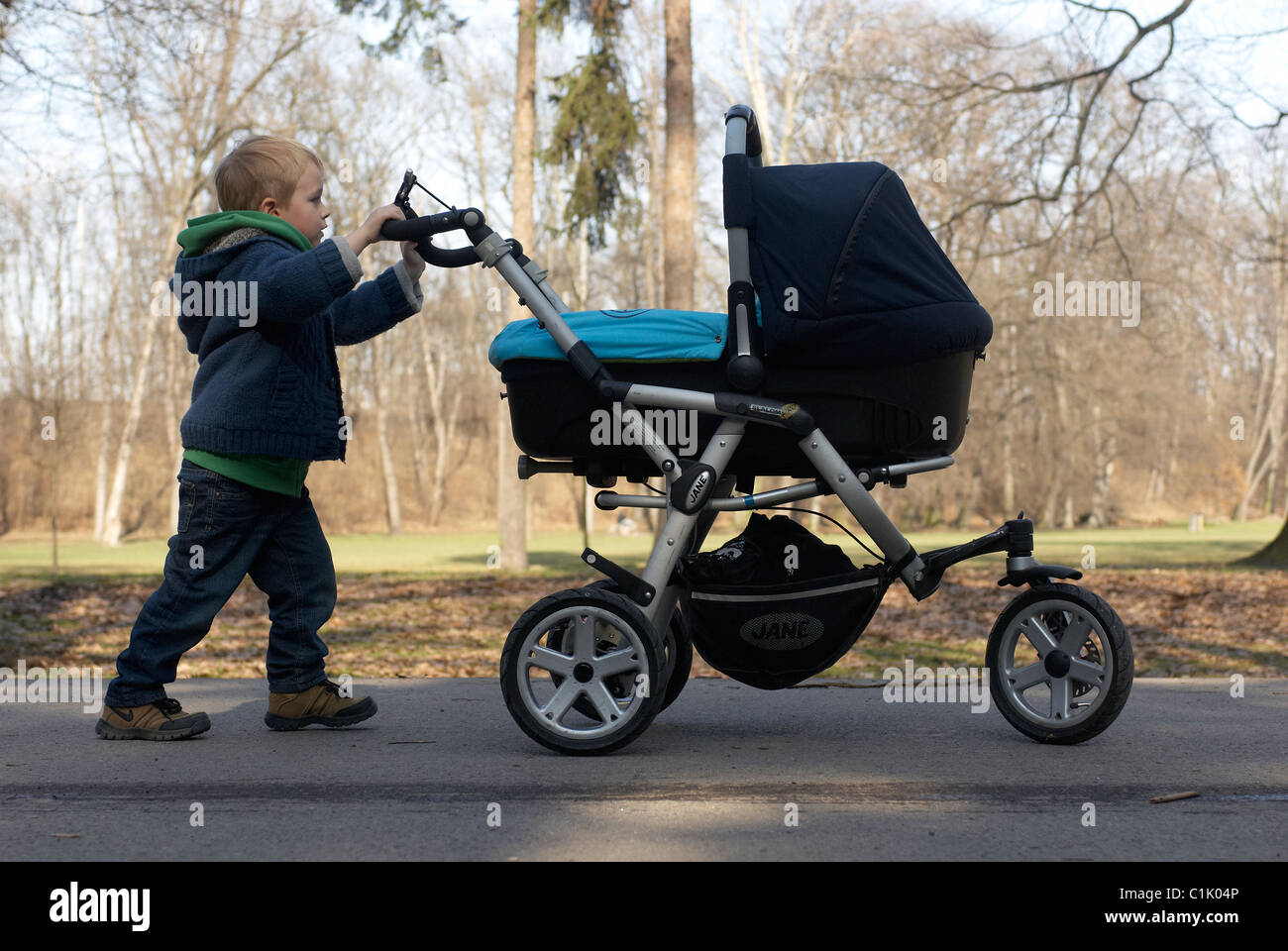 Child blond boy pushing stroller with sister in park Stock Photo - Alamy