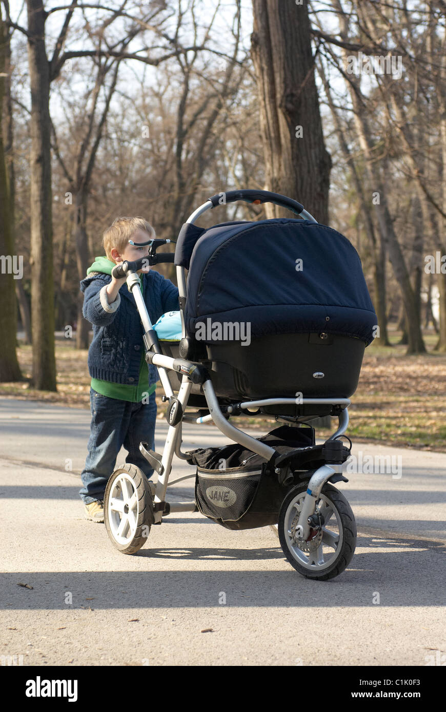 Child blond boy pushing stroller with sister in park Stock Photo - Alamy