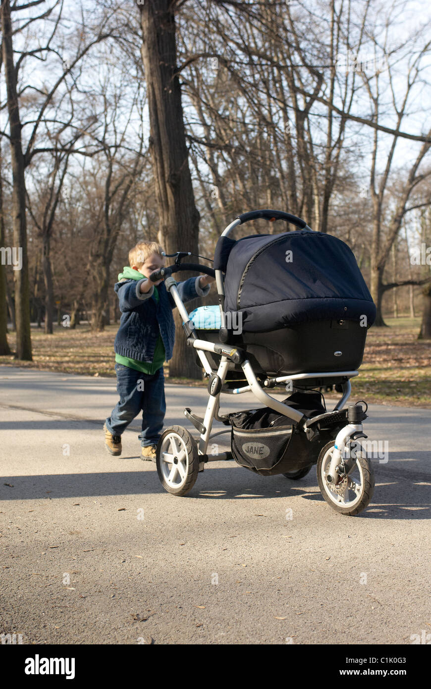 Child blond boy pushing stroller with sister in park Stock Photo - Alamy