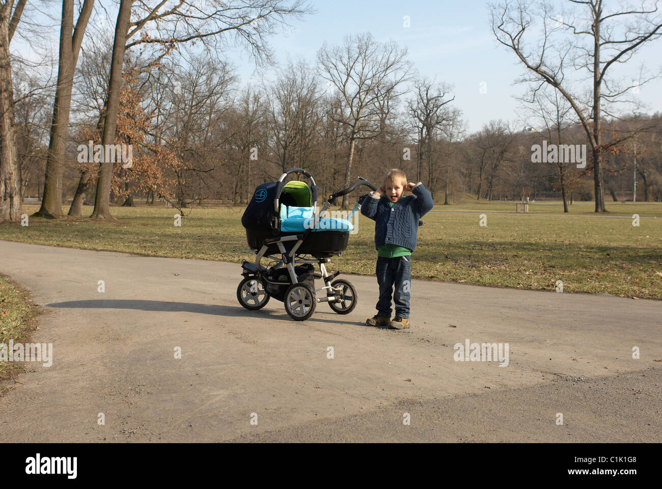 Child blond boy pushing stroller with sister in park Stock Photo - Alamy