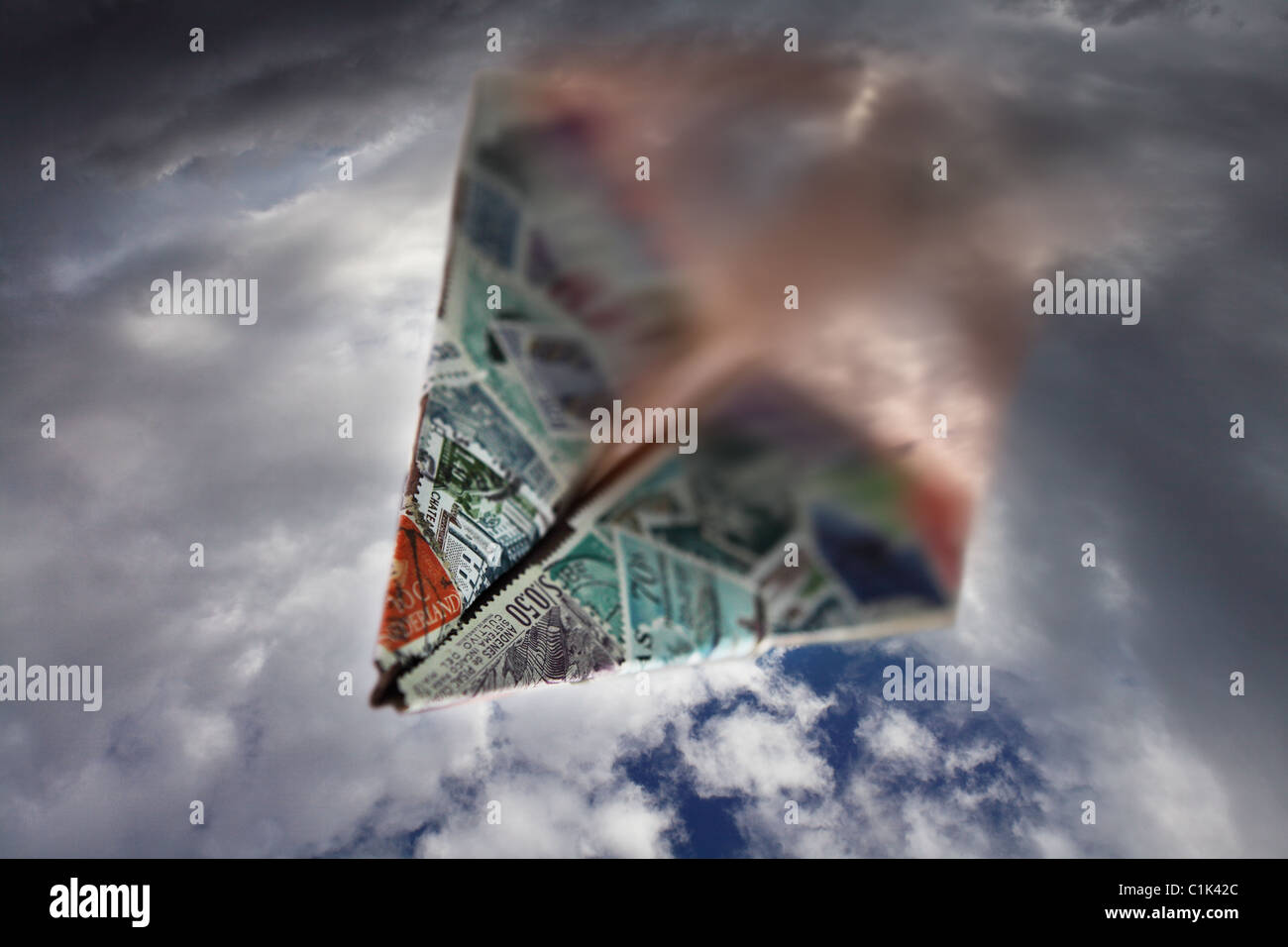 paper postage stamp airplane flying fast and high above the clouds ...