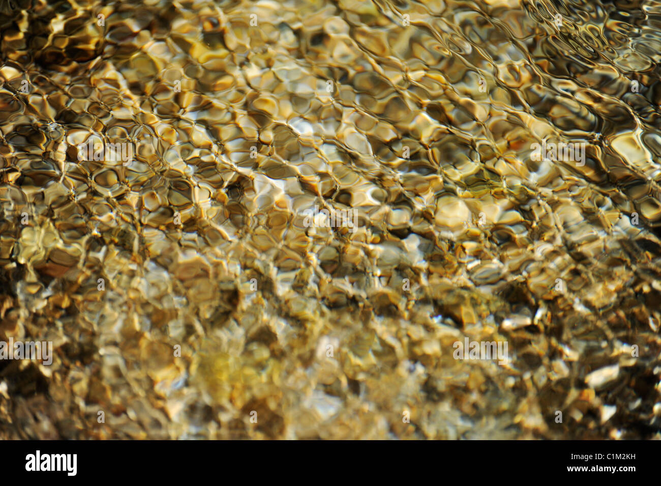 Close-up of water rippling over pebbles in a shallow part of river ...