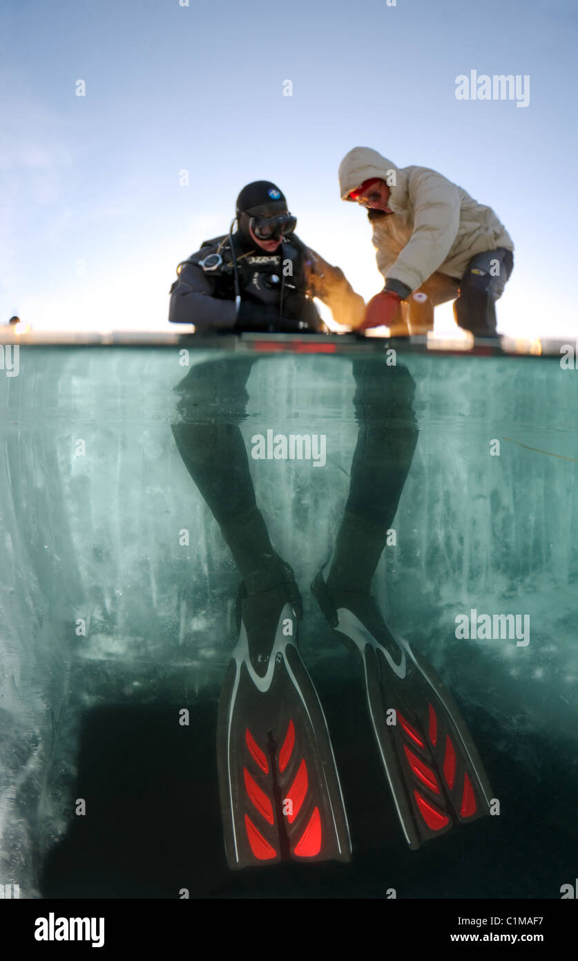 Split level, ice-diver sits on the ice in lake Baikal, Siberia, Russia ...