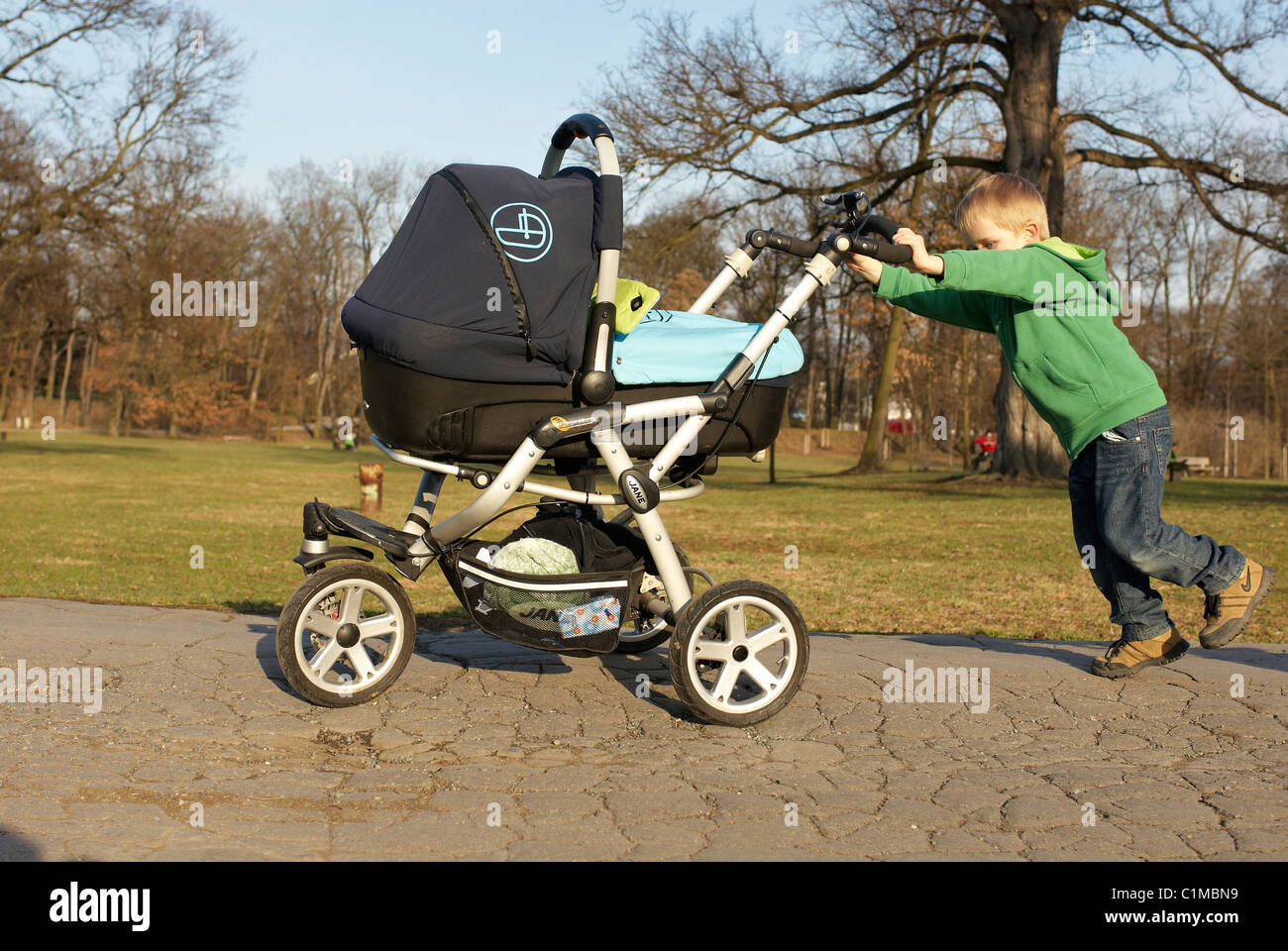 Child blond boy pushing stroller with sister in park Stock Photo - Alamy