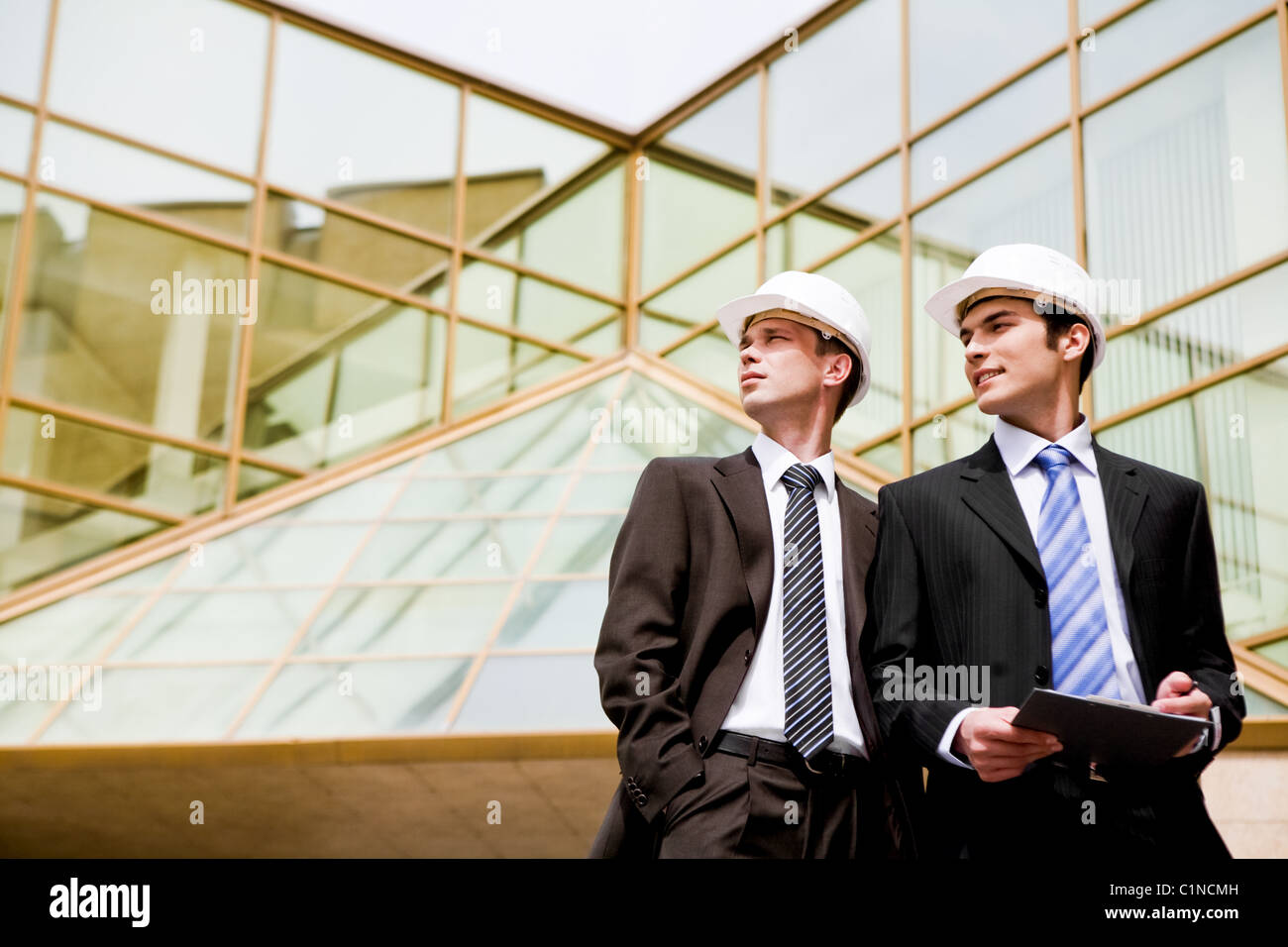 Photo of young engineers looking aside with modern building at ...