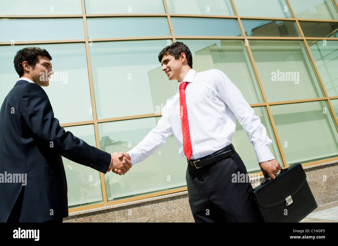 Image of two confident males handshaking outdoors at background of ...