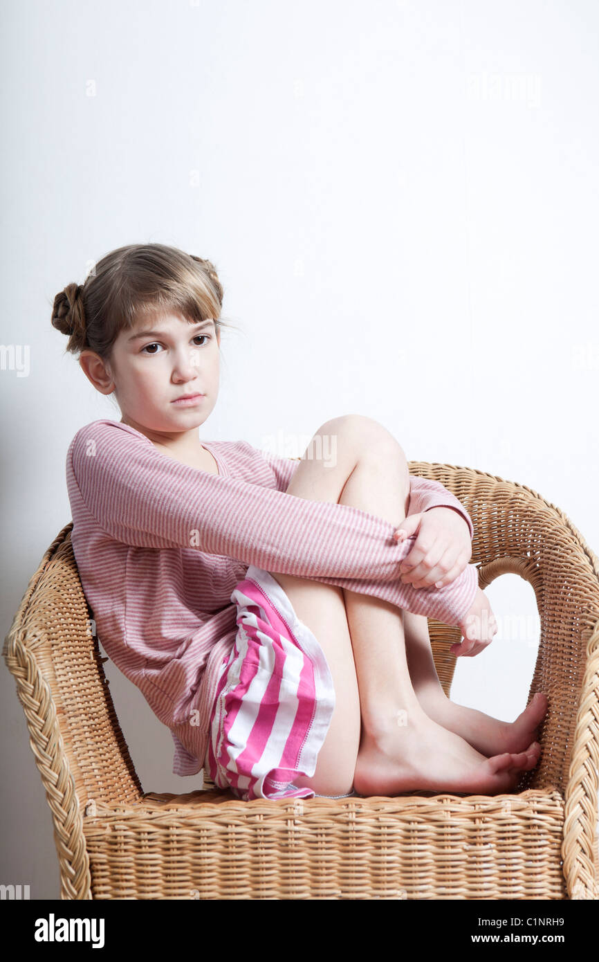 Calm little girl sitting on chair and looking ahead Stock Photo - Alamy