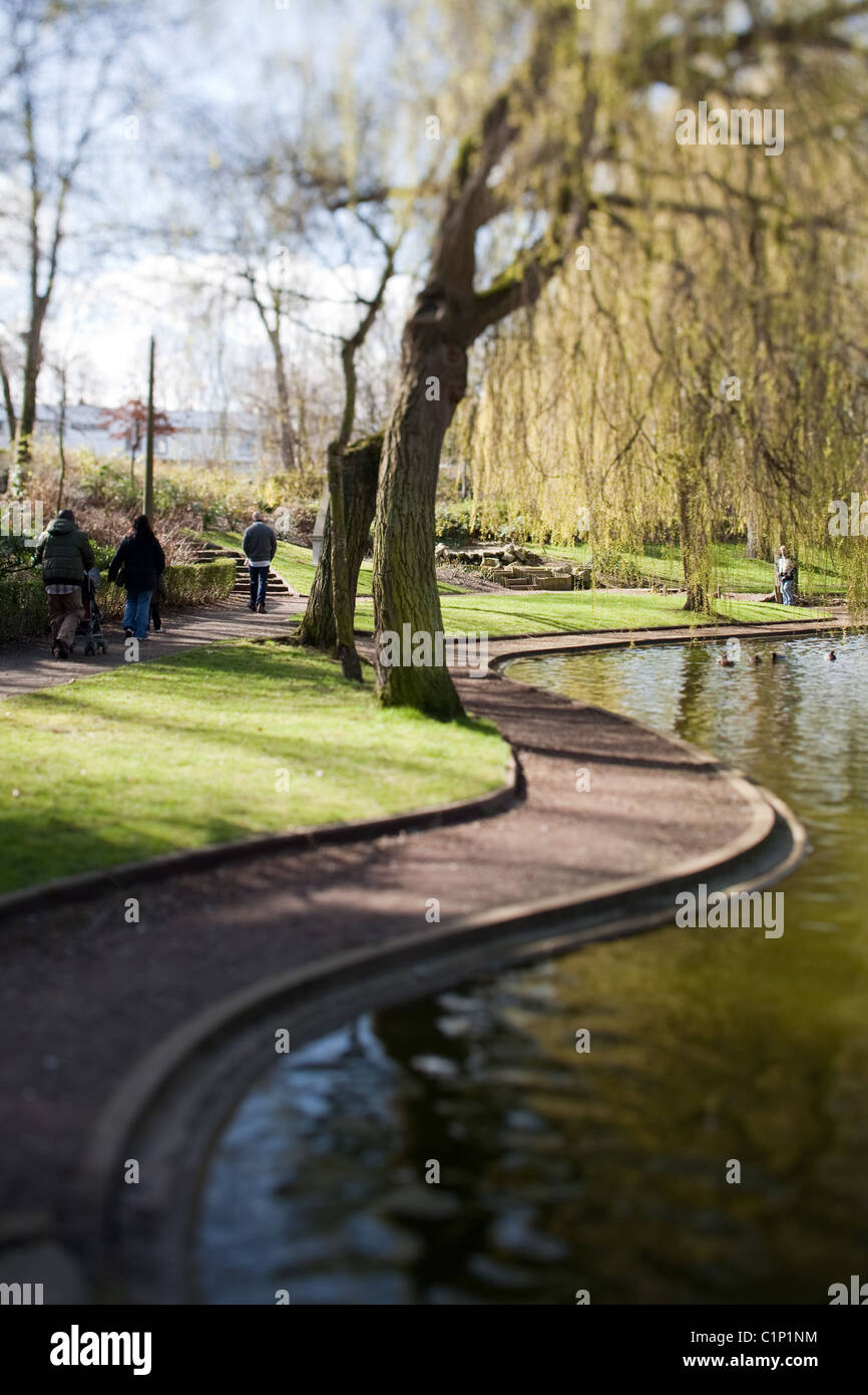 People strolling in a park with green grass and a pond, meandering path ...