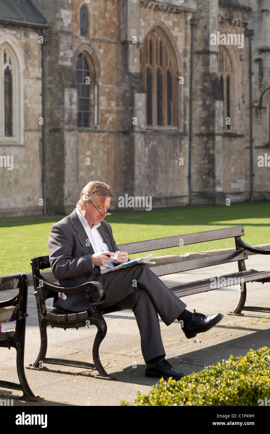 man eating lunch on bench in the sunshine in front of the cathedral in ...