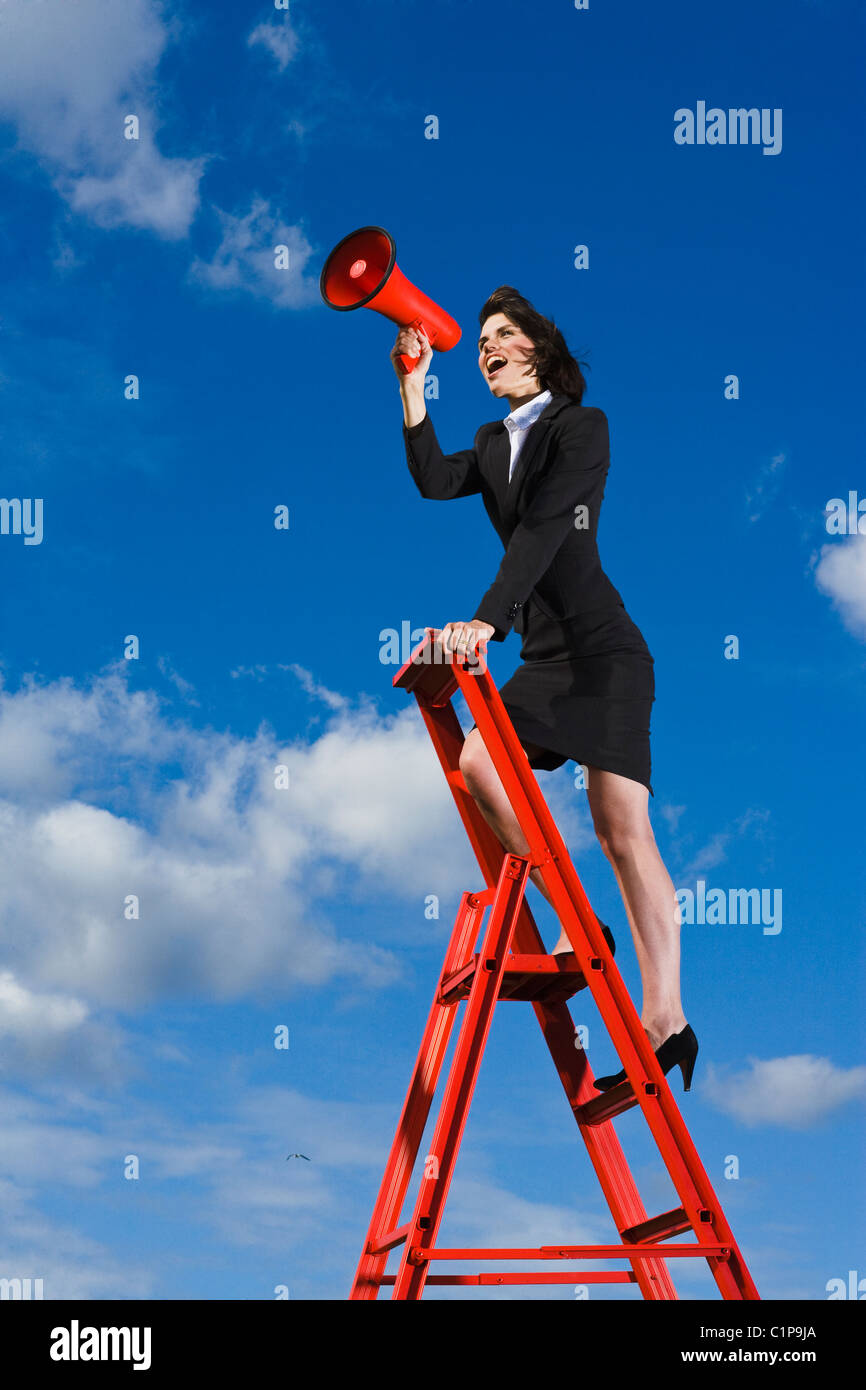 Businesswoman standing on top of red ladder against blue sky and ...