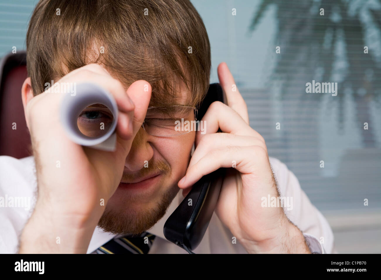 Close-up of playful man with paper roll by his eye while speaking on ...