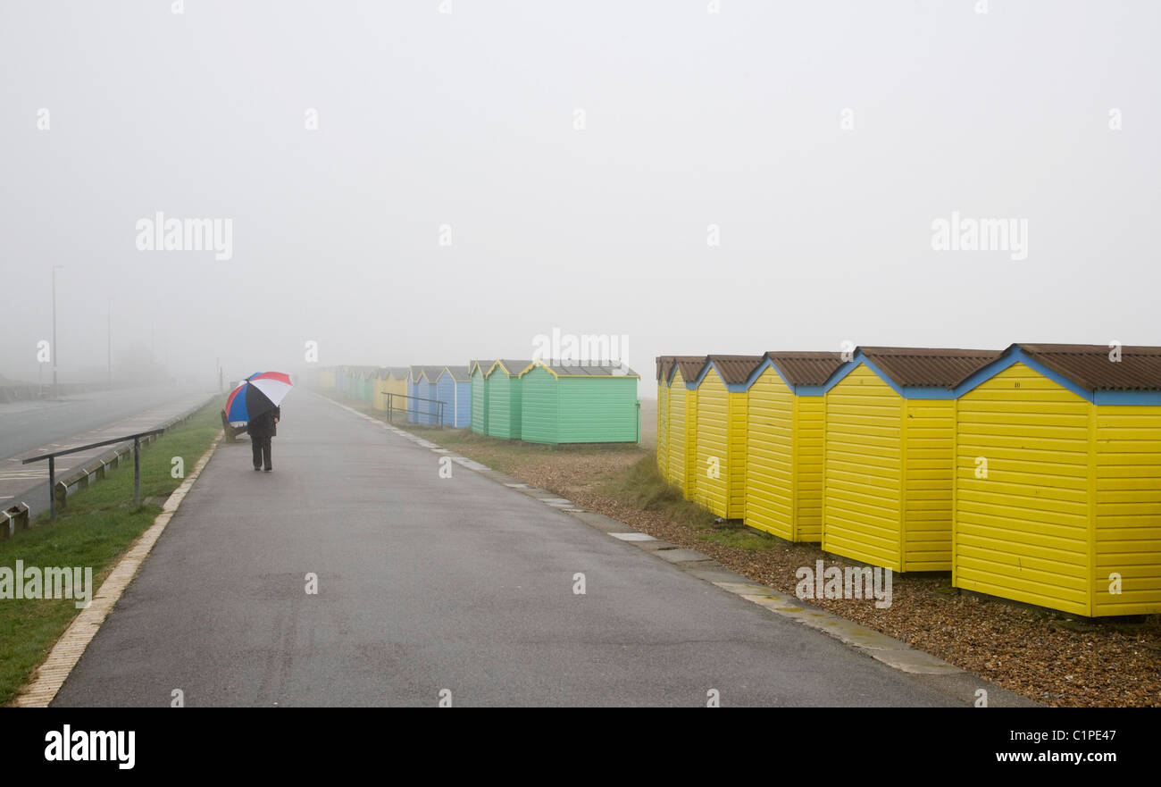 A lady walking past beach huts on a rainy misty day Stock Photo - Alamy