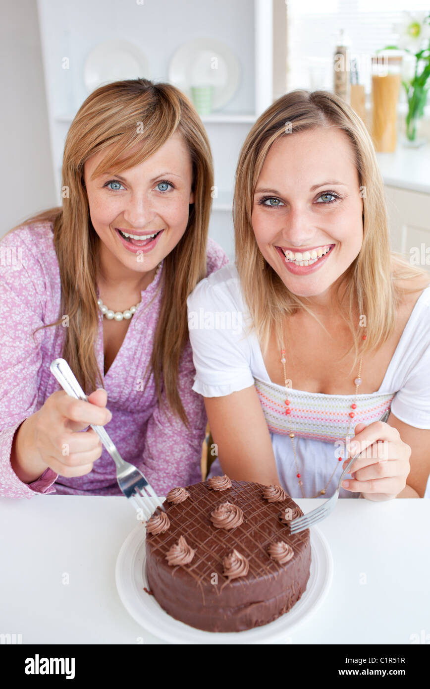 Happy friends with a cake smiling at the camera sitting in the kitchen ...