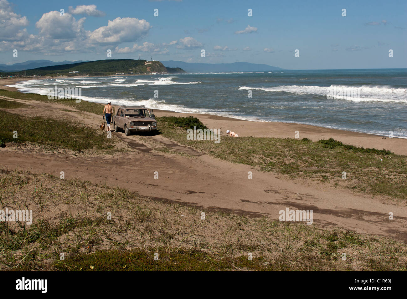 A man stands by his car by the beach in Okhotsk, Sakhalin, Russia ...
