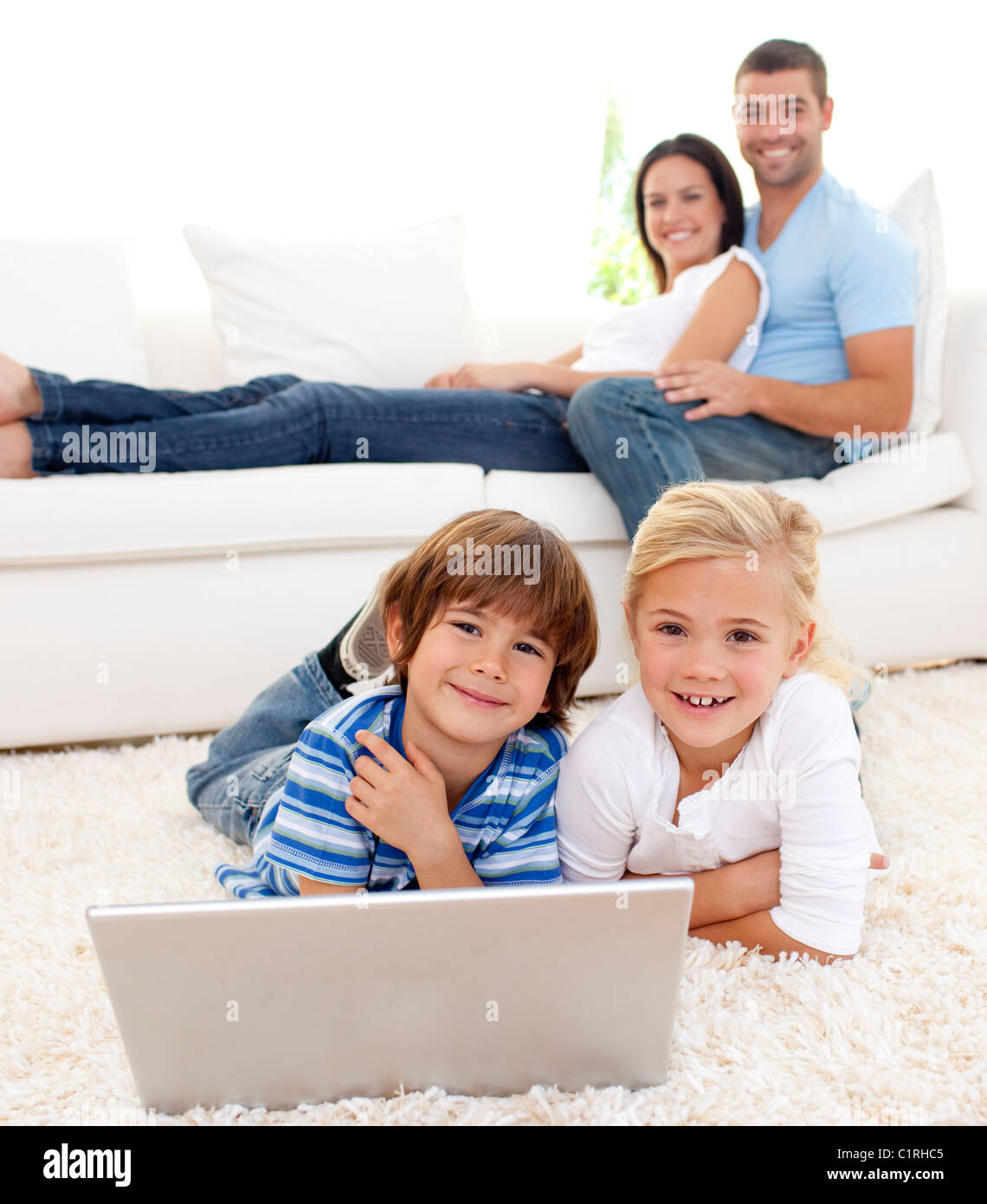 Children playing with a laptop and parents lying on sofa Stock Photo ...